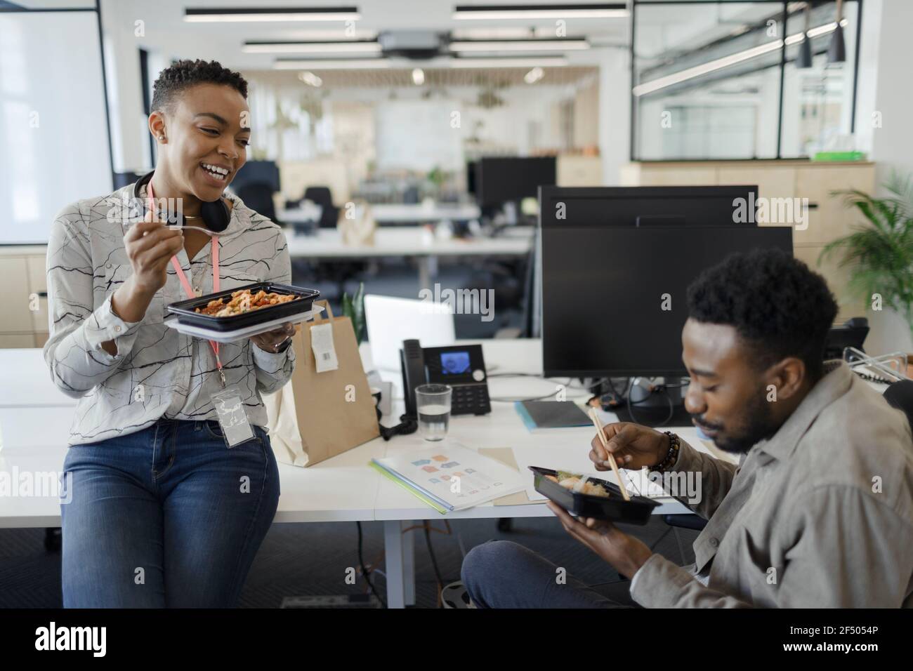 Happy business people eating takeout lunch at desk in open plan office ...