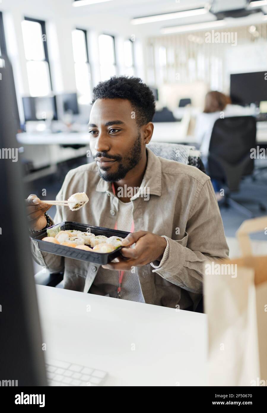 Businessman eating takeout sushi lunch at computer in office Stock ...