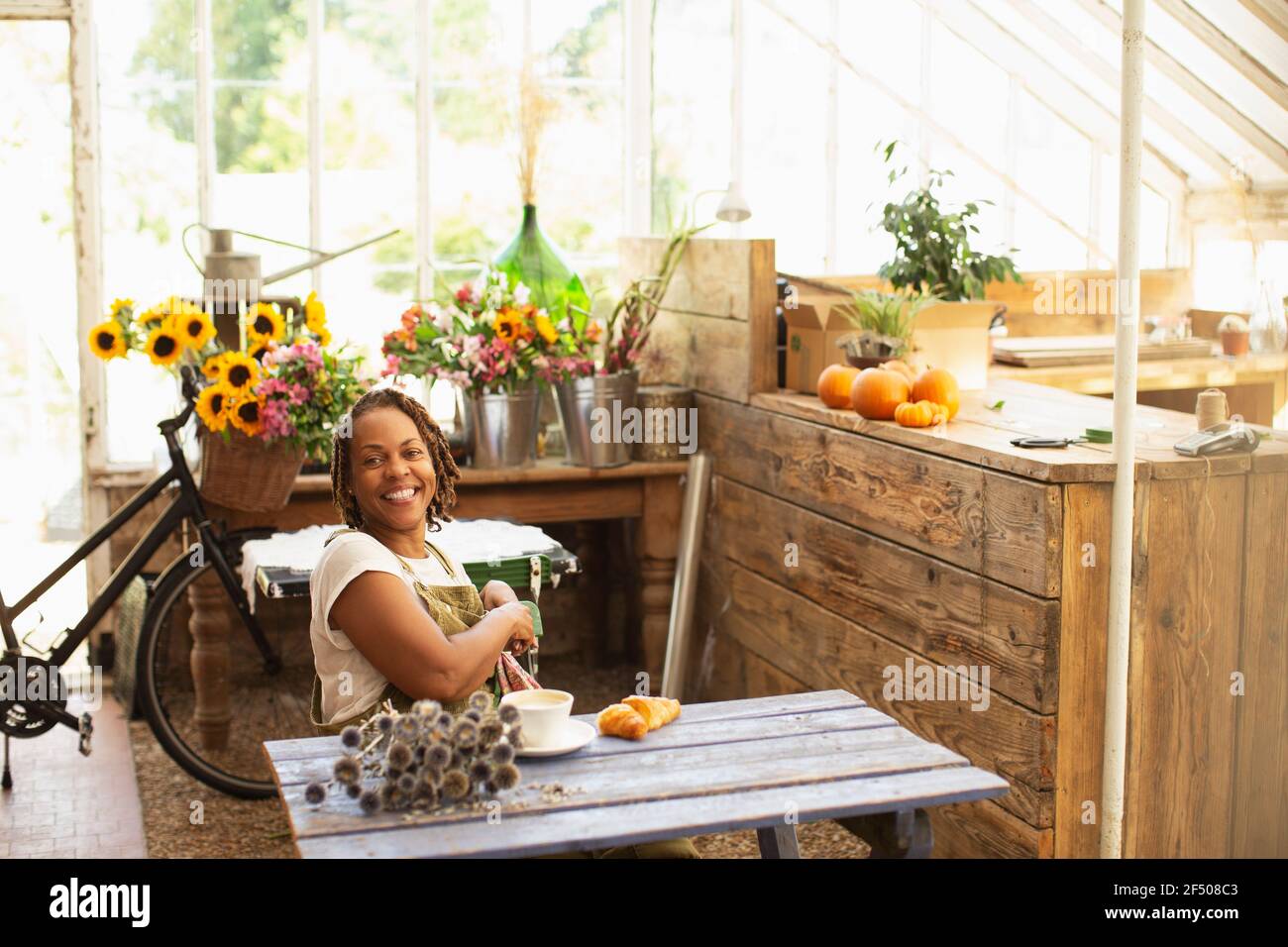 Portrait happy female florist enjoying coffee break in flower shop ...