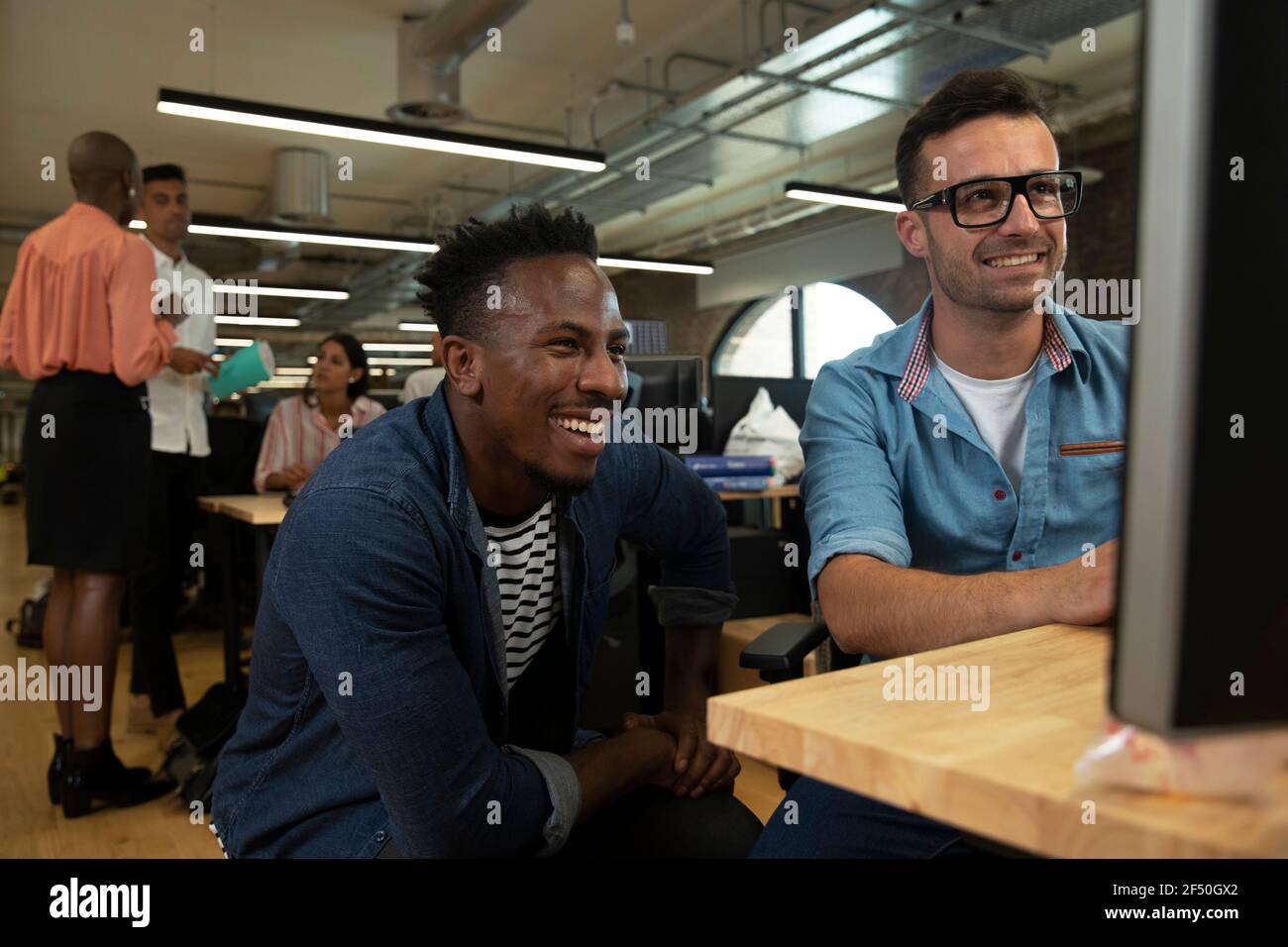 Happy businessmen working at computer in open plan office Stock Photo ...