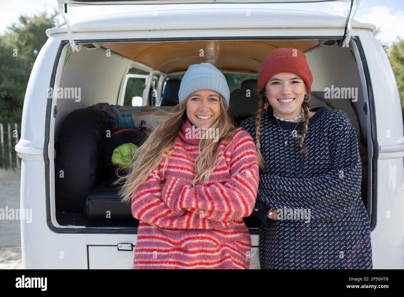 Portrait happy young women friends in knit hats at back of camper van ...