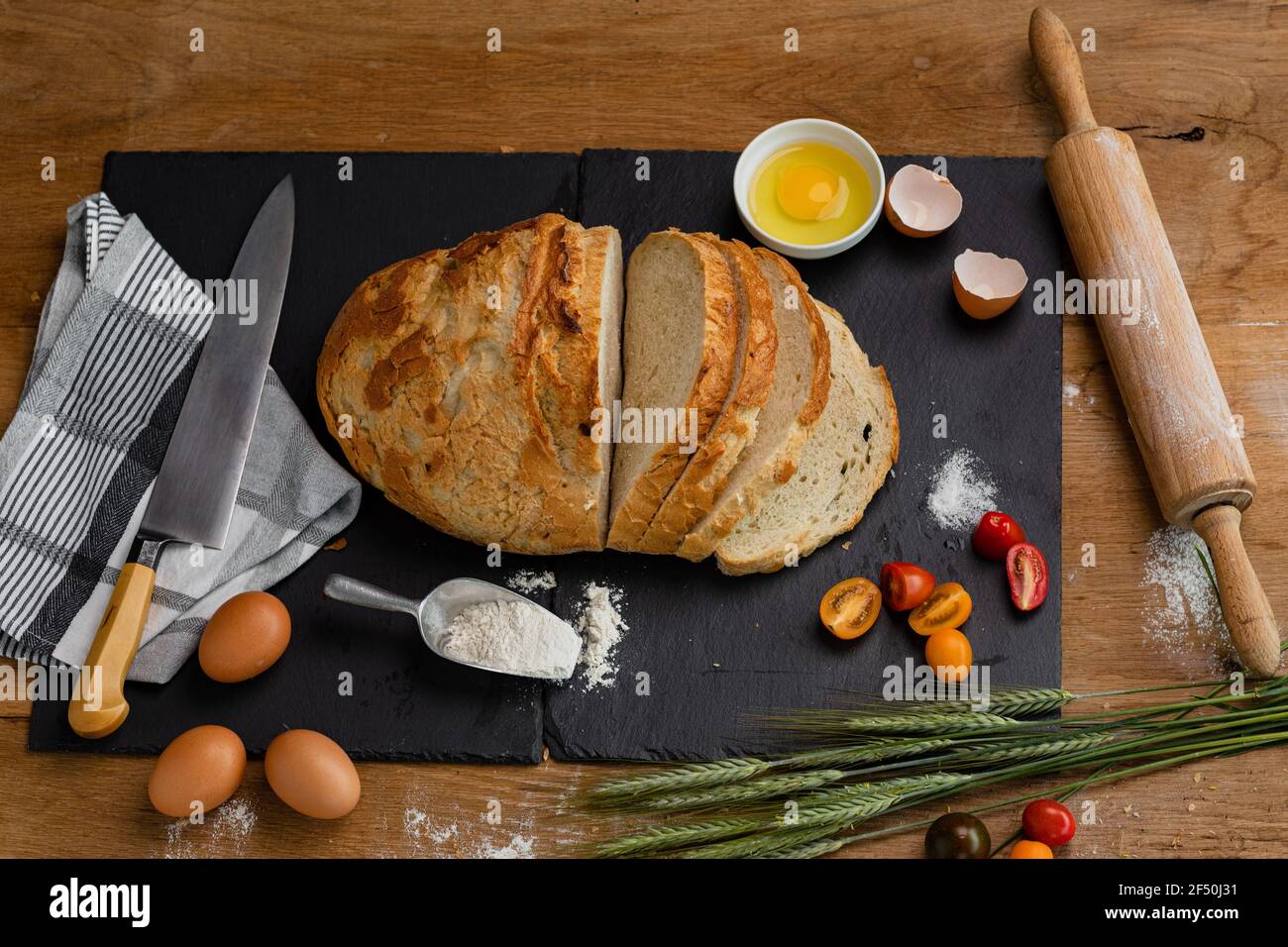 Gold rustic crusty loaves of bread on a blackstone board with tomatoes ...