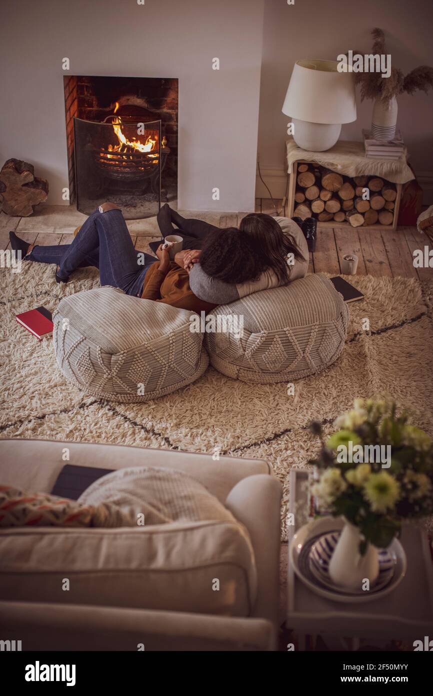 Affectionate mother and daughter cuddling by fireplace with coffee ...