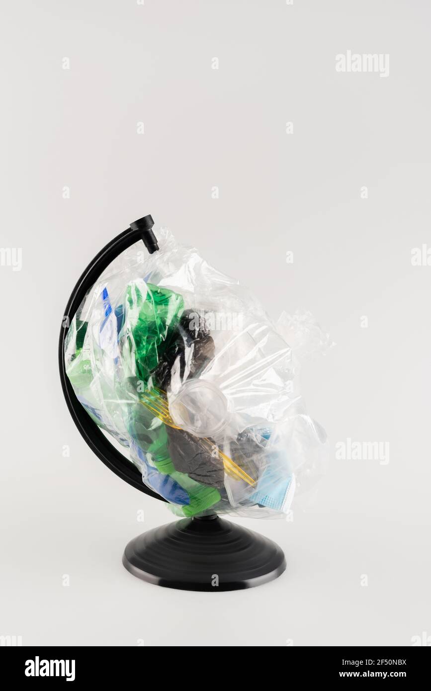 cellophane pack with plastic garbage on globe stand isolated on grey ...
