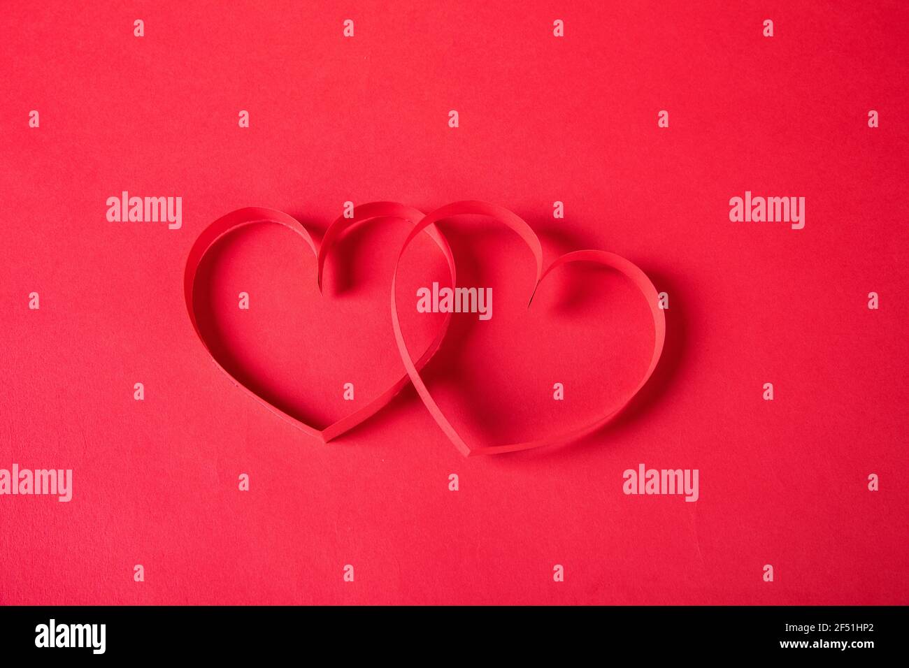 Top view of two heart shape paper cutouts isolated on a red background ...