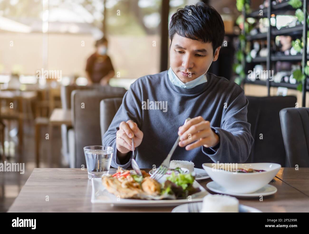 young man with face mask eating a food in restaurant, New normal ...