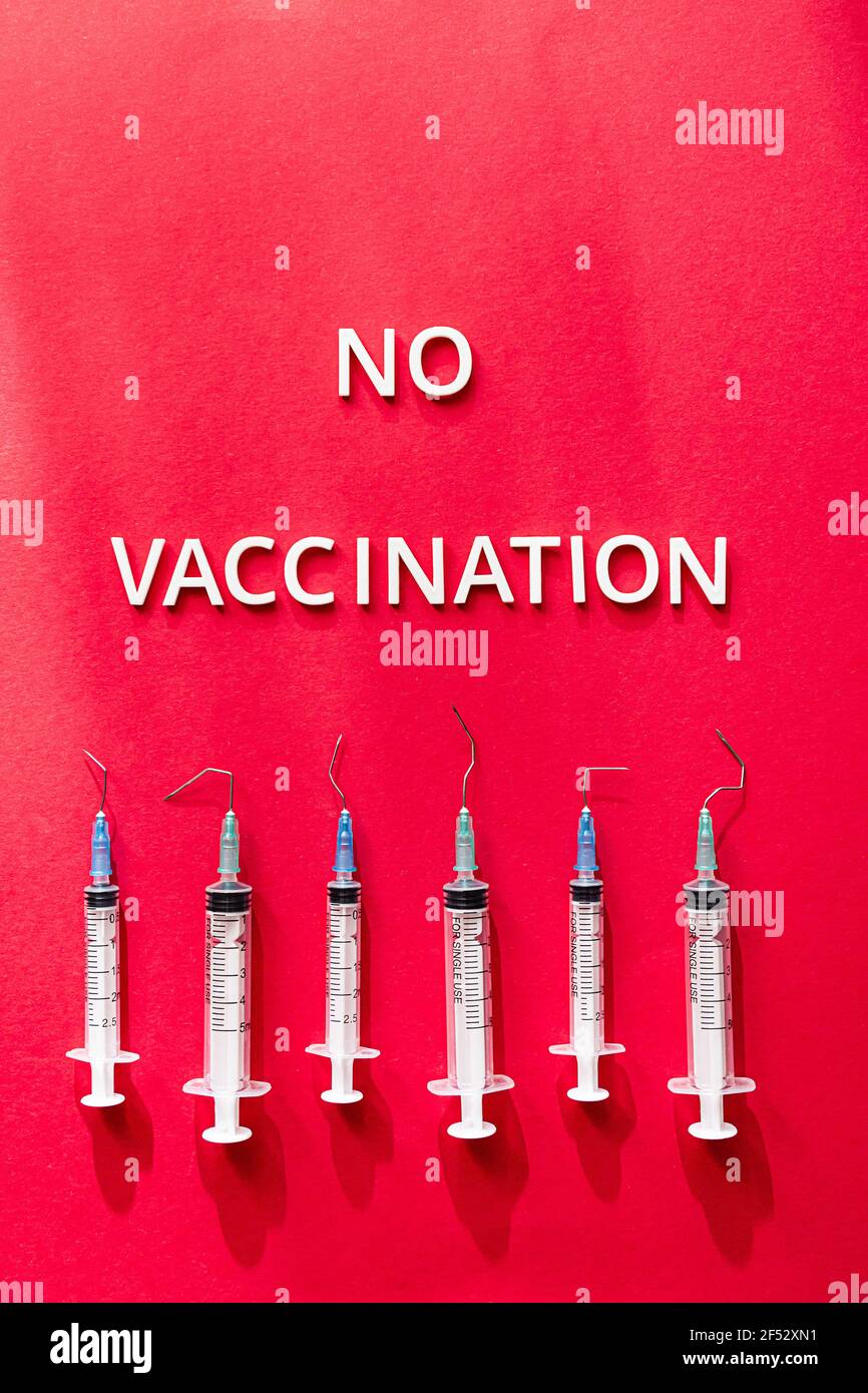 The phrase "NO VACCINATION", broken injection syringes on a red ...