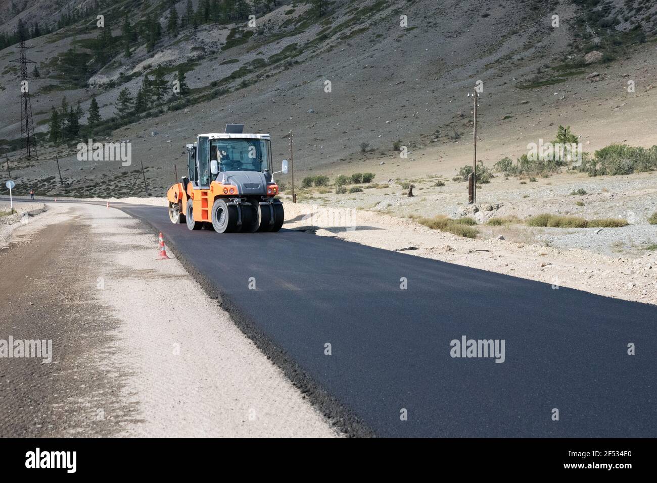 Asphalt paver of orange color rolls black asphalt for a road in the ...