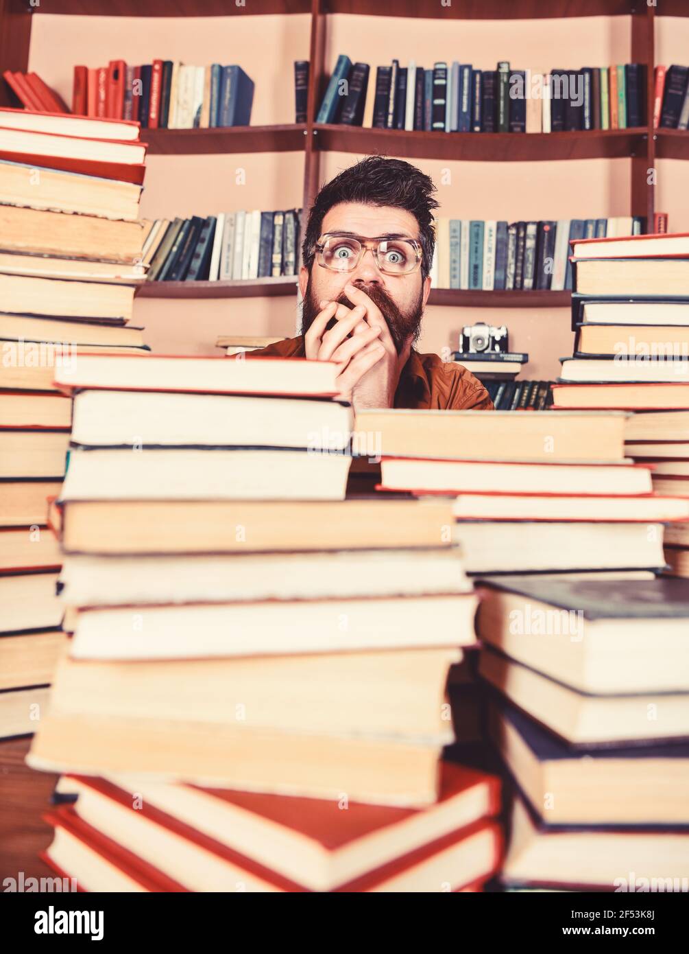 Man on shocked face between piles of books in library, bookshelves on ...