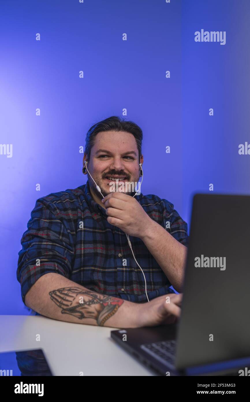Bearded Spanish man with a big tattoo on his arm using earphones while ...