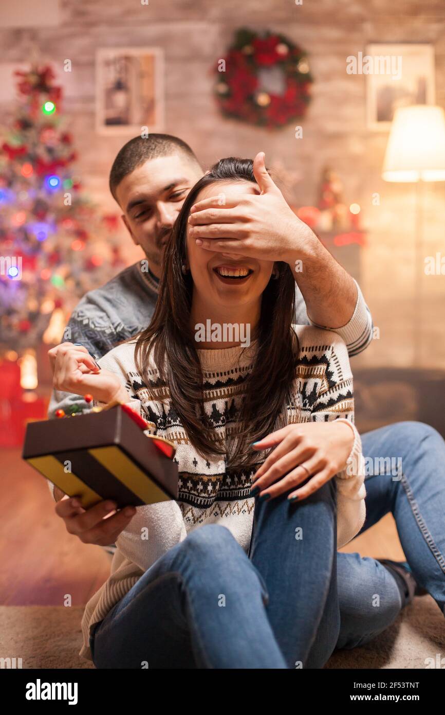 Smiling girlfriend with eyes covered receiving her christmas gift from ...