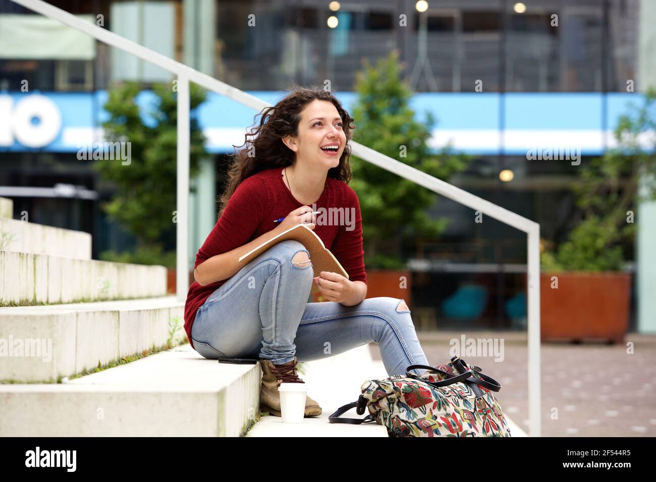 Portrait of attractive young woman sitting on steps with notebook and ...