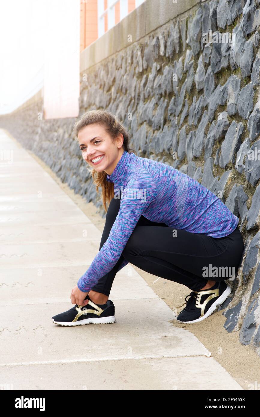 Full body portrait of athletic woman tying sneaker on sidewalk Stock ...