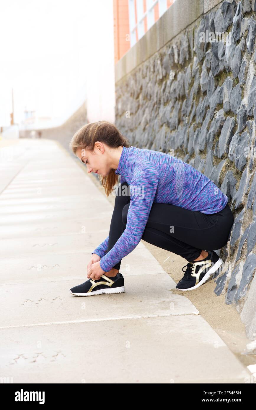 Full body portrait of athletic woman tying sneaker on path Stock Photo ...