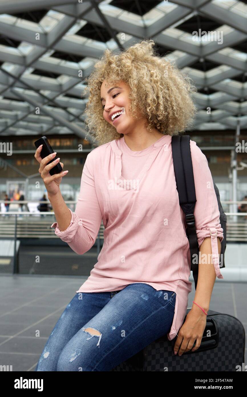 Portrait of young african american woman sitting on suitcase with ...