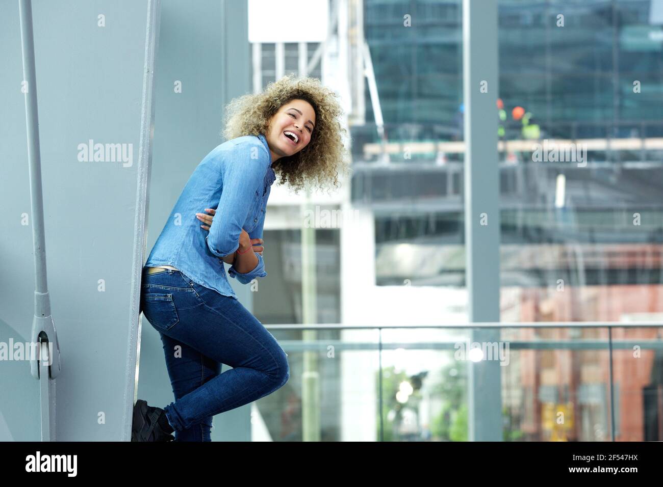 Portrait of laughing woman with arms crossed leaning on wall Stock ...