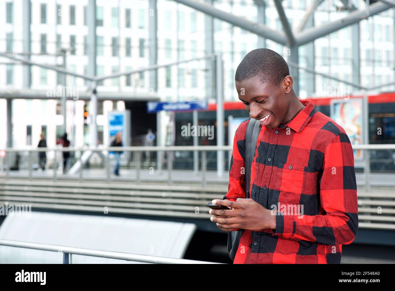 Portrait of cheerful young black guy at railway station reading text ...