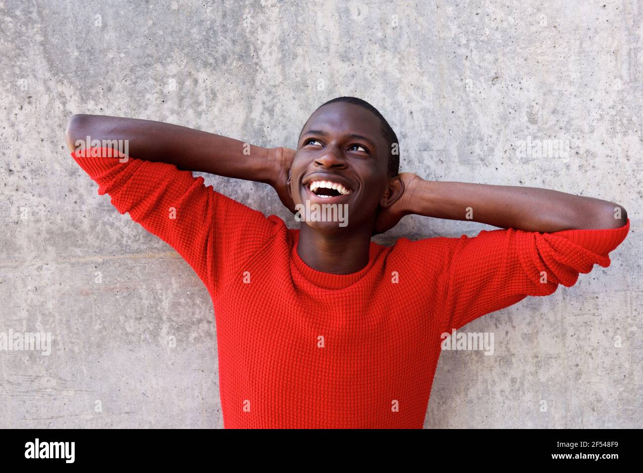 Close up portrait of smiling black guy standing with hands behind head and looking up Stock ...