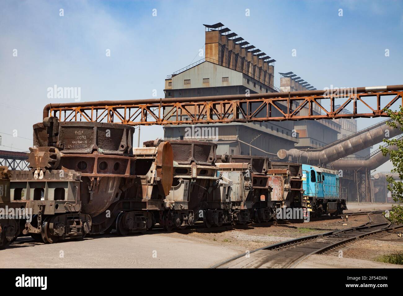 Metal alloys plant. Rusted slag cars and blue locomotive on rails ...