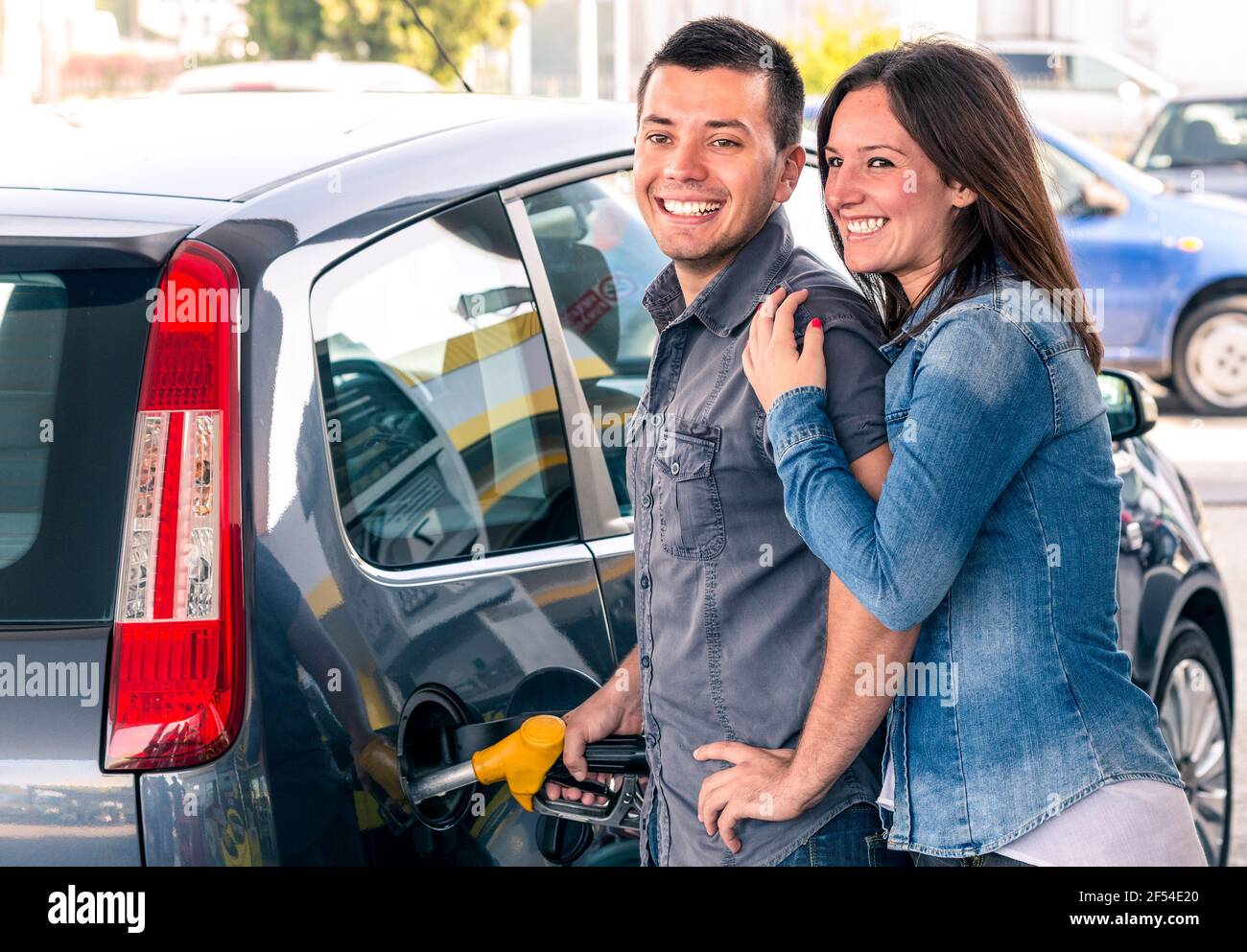 Happy couple at fuel station pumping gasoline at gas pump. Portrait of ...