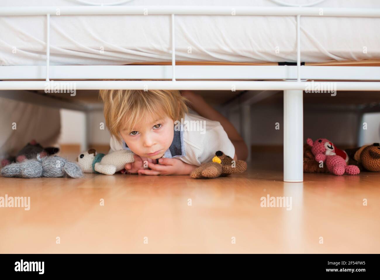 Little toddler child, hiding under the bed with stuffed toys, scared ...