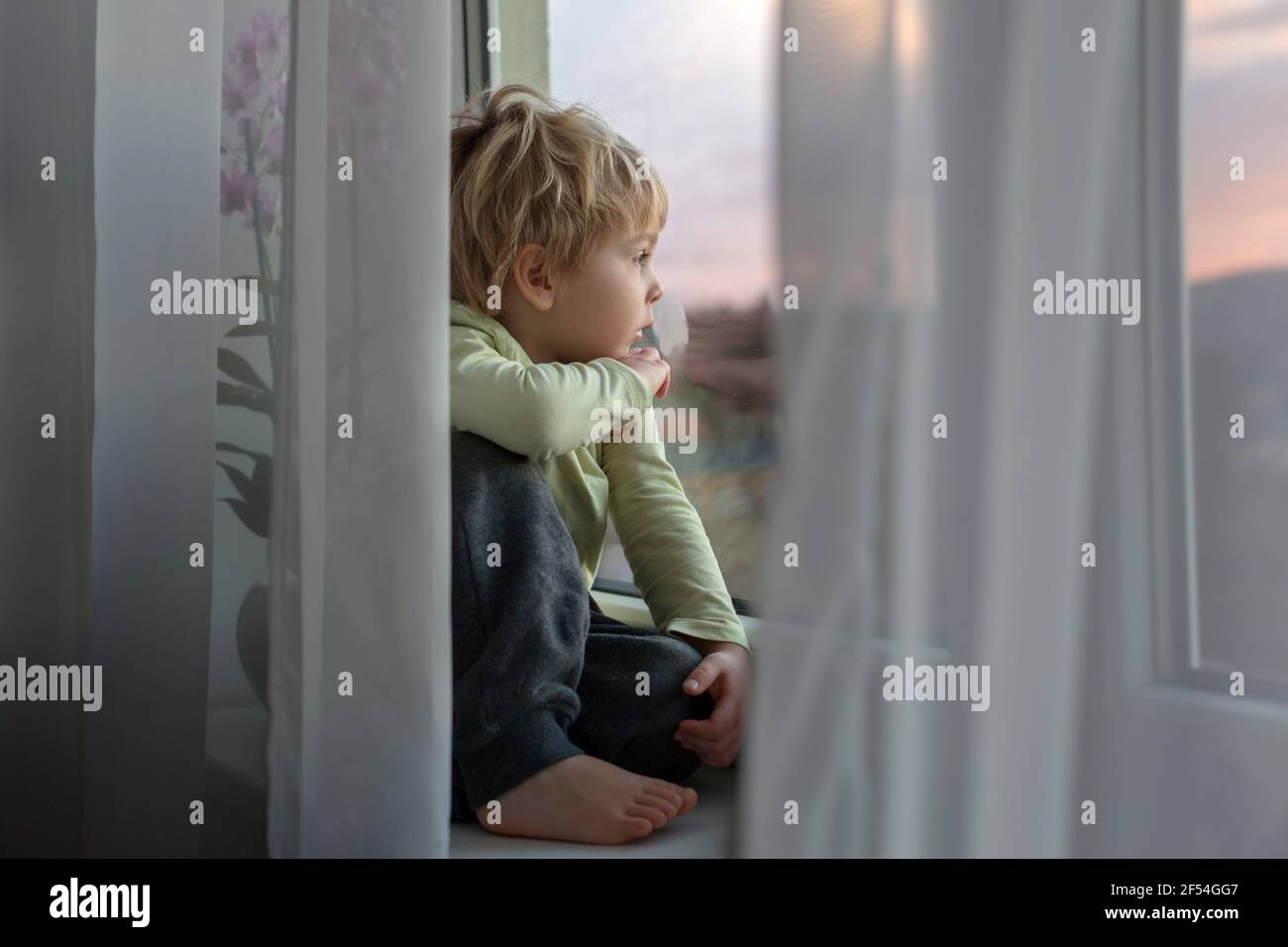 Blond toddler child, sitting on the window on sunset, looking out Stock ...