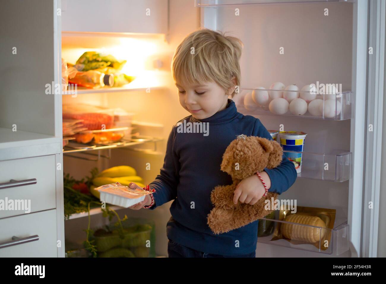Cute toddler blond child, opening the fridge doorand taking out white ...