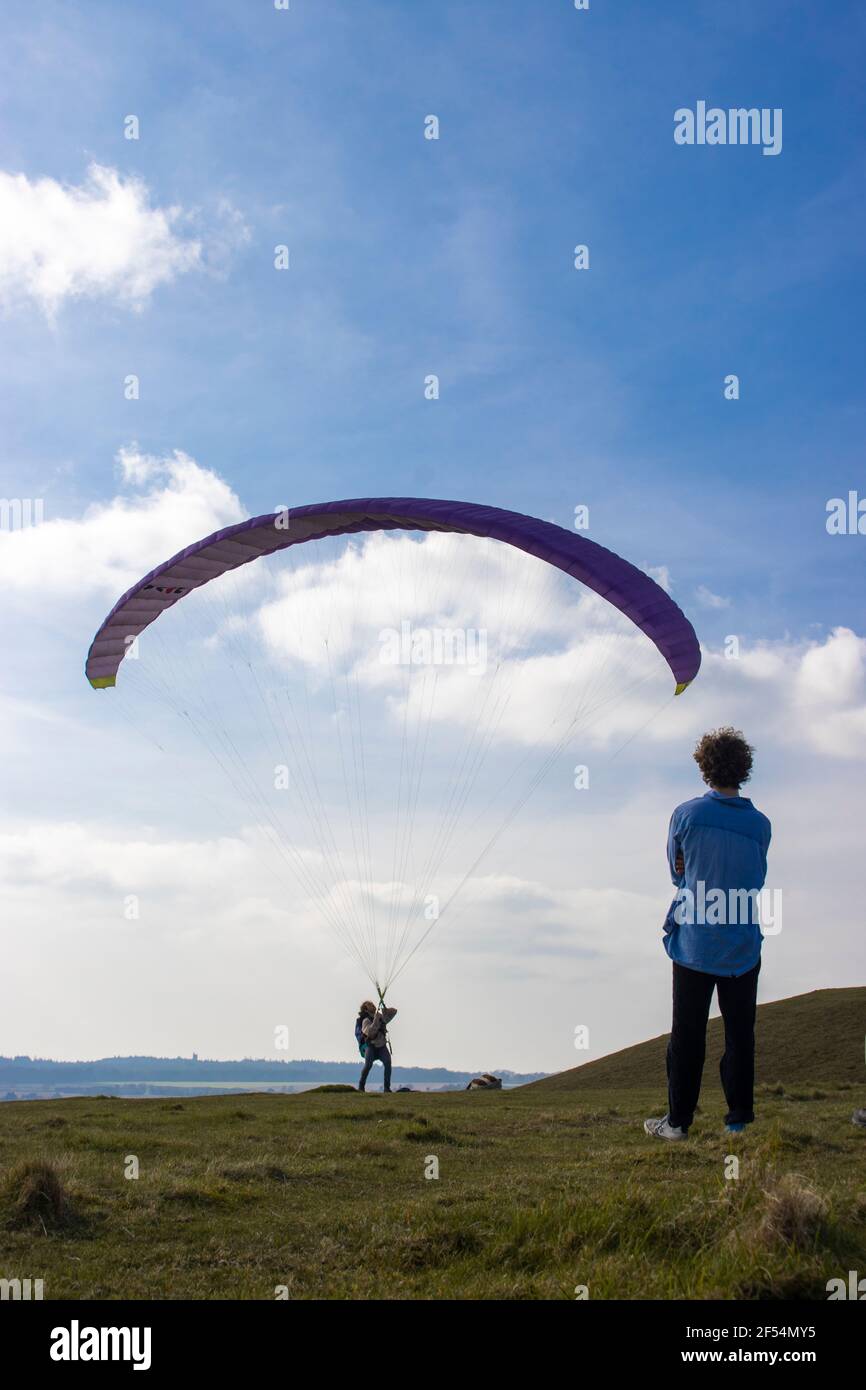 A paraglider taking off from a green hill with an observer watching ...