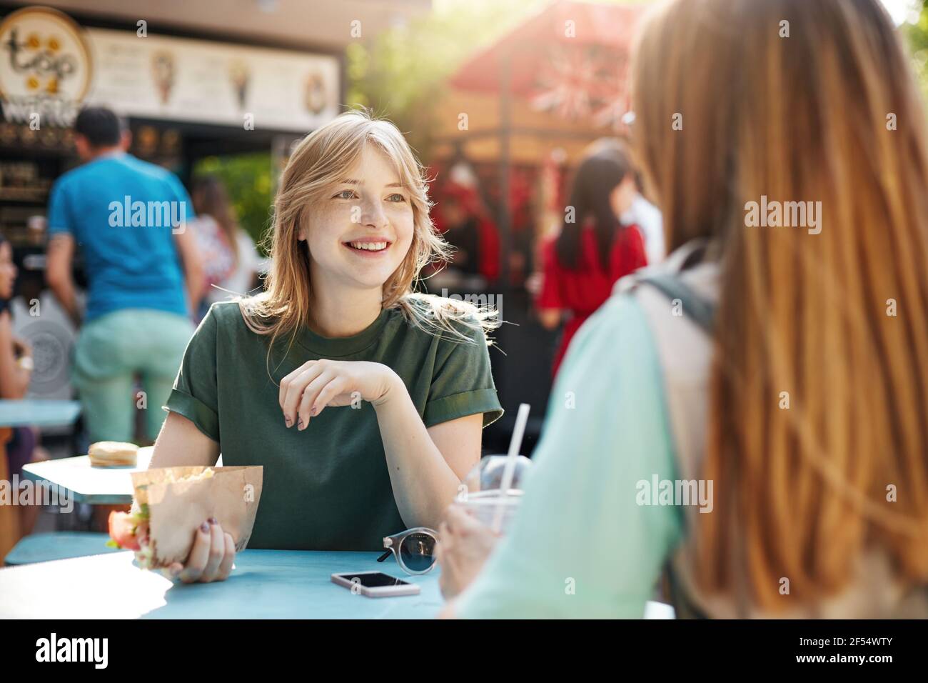 Best friends chatting on a sunny day eating tacos in park or a faire ...