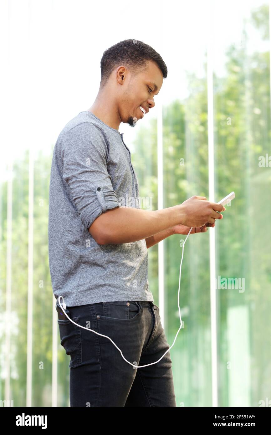 Side portrait of smiling man standing and using smart phone outside ...
