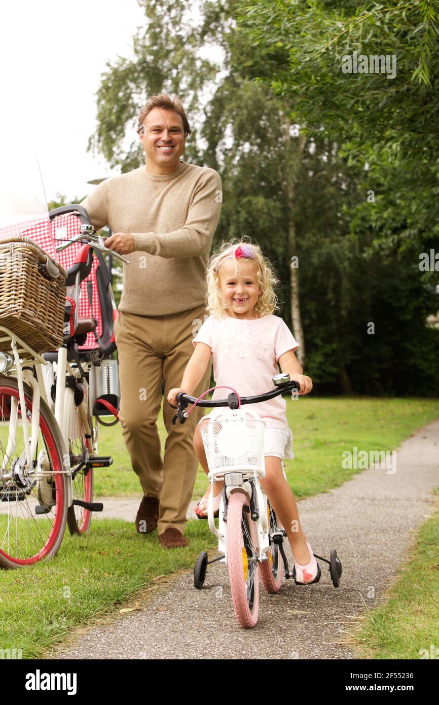 Full length portrait of father and daughter cycling together in park ...