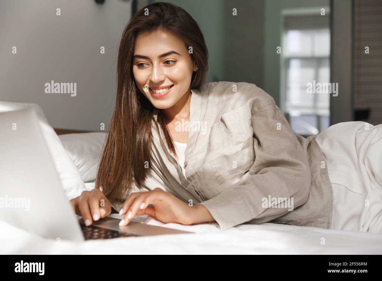 Happy woman lying in bed with laptop and browsing internet. Girl ...