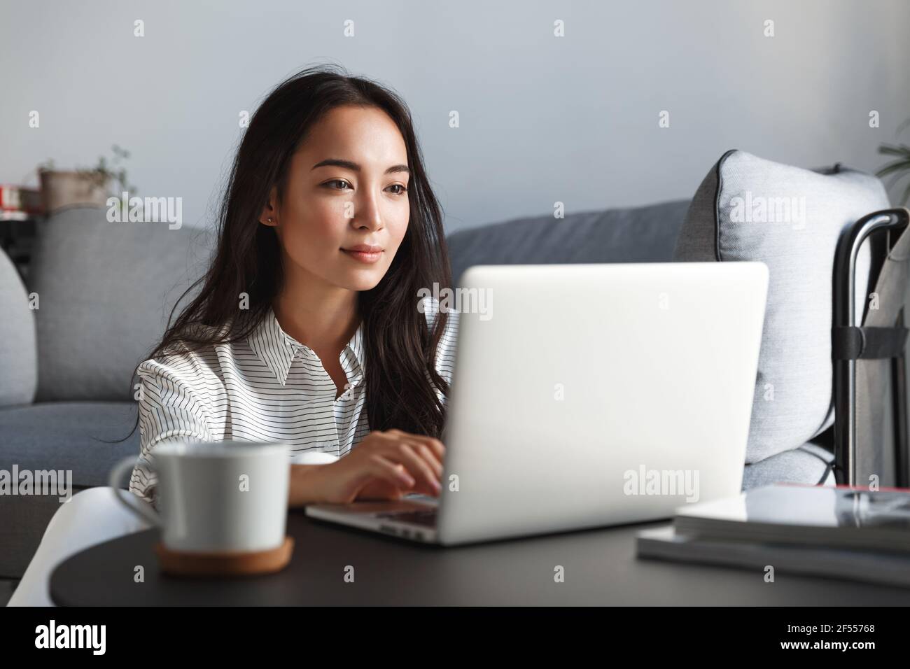 Young ambitious asian girl working remote from home, looking at laptop ...