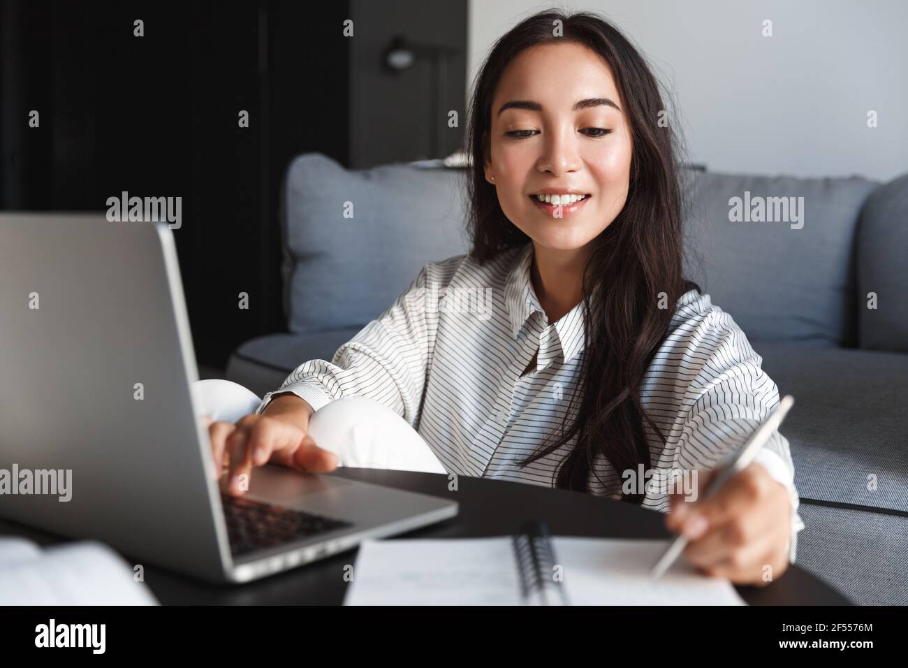 Image of beautiful asian girl studying remote from home, writing down ...
