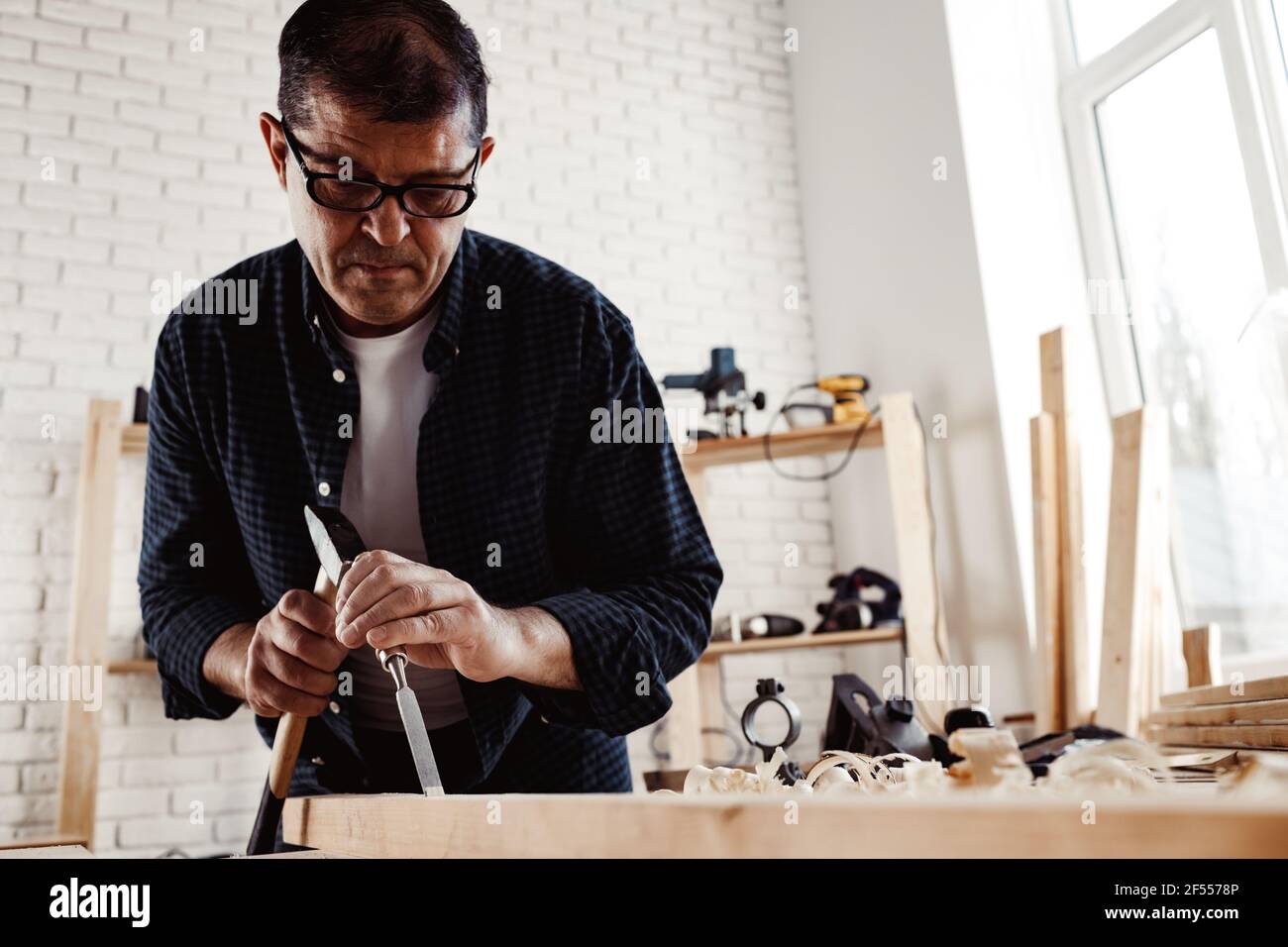 Middle-aged man carpenter working in a workshop with chisel and hammer ...