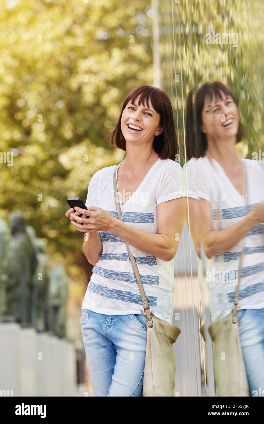 Portrait of happy older woman leaning against reflection in building ...