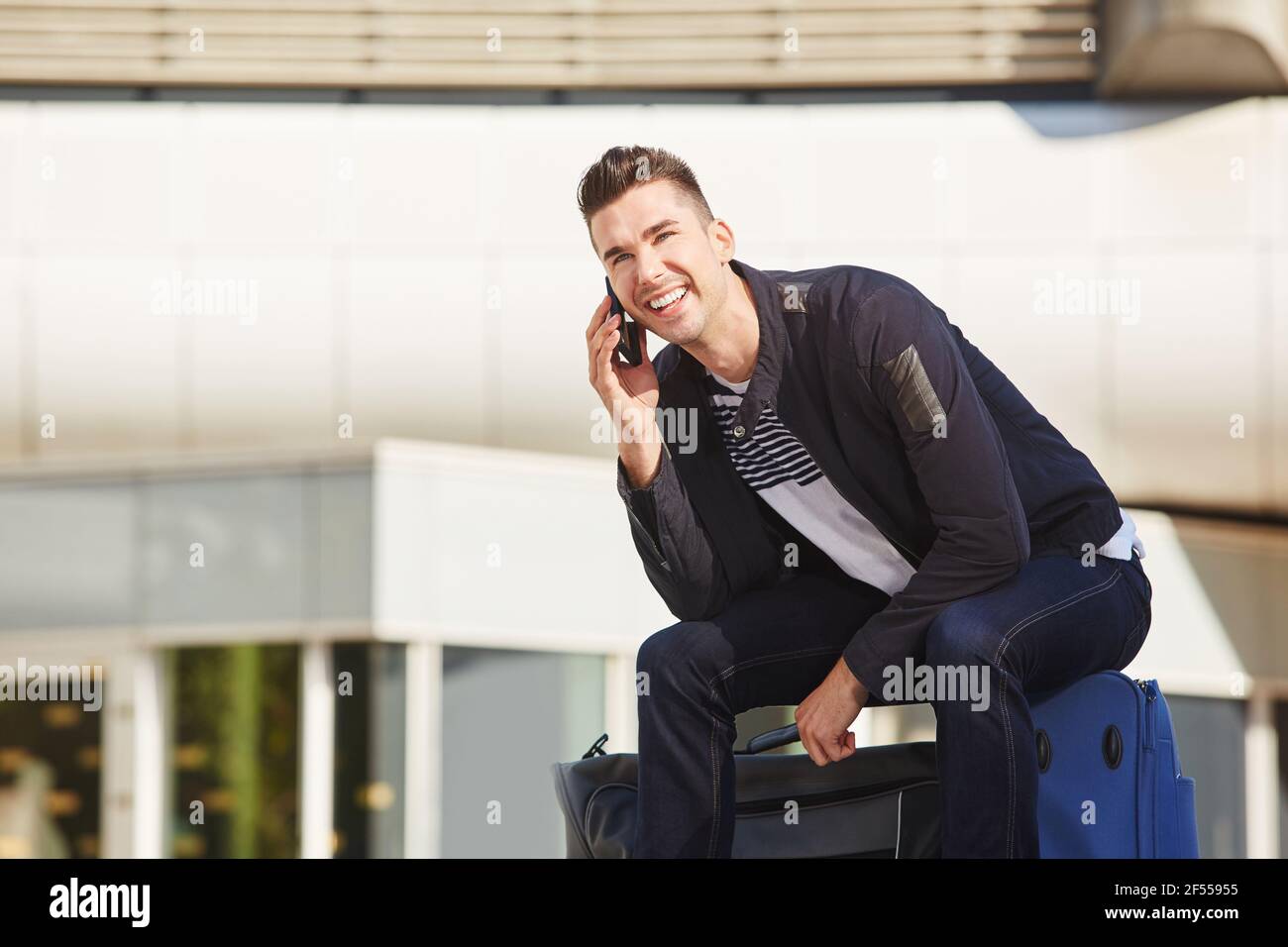 Portrait of smiling man waiting at station with luggage on phone call ...