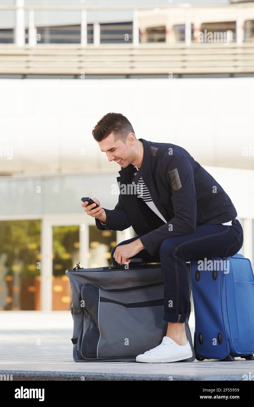 Full body portrait of smiling man waiting with luggage and phone at ...