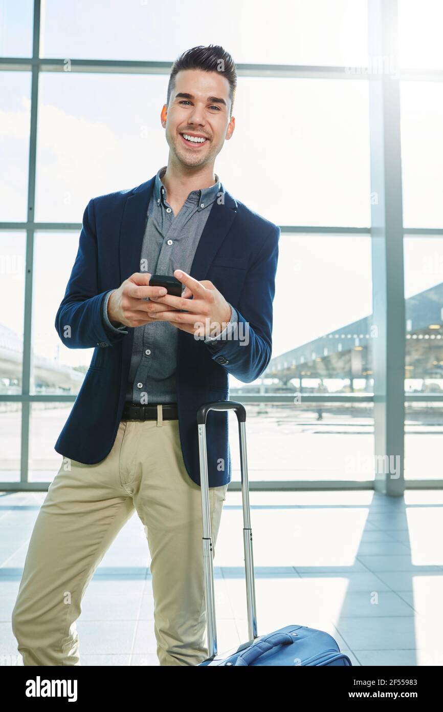 Portrait of smiling man standing in station with suitcase and smart ...