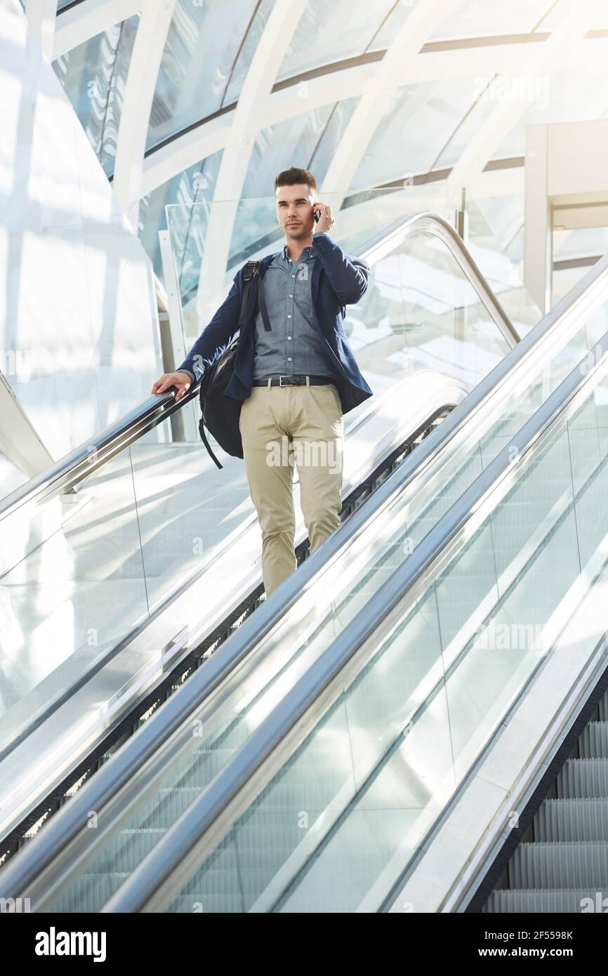 Portrait of serious business man standing on escalator on mobile phone ...