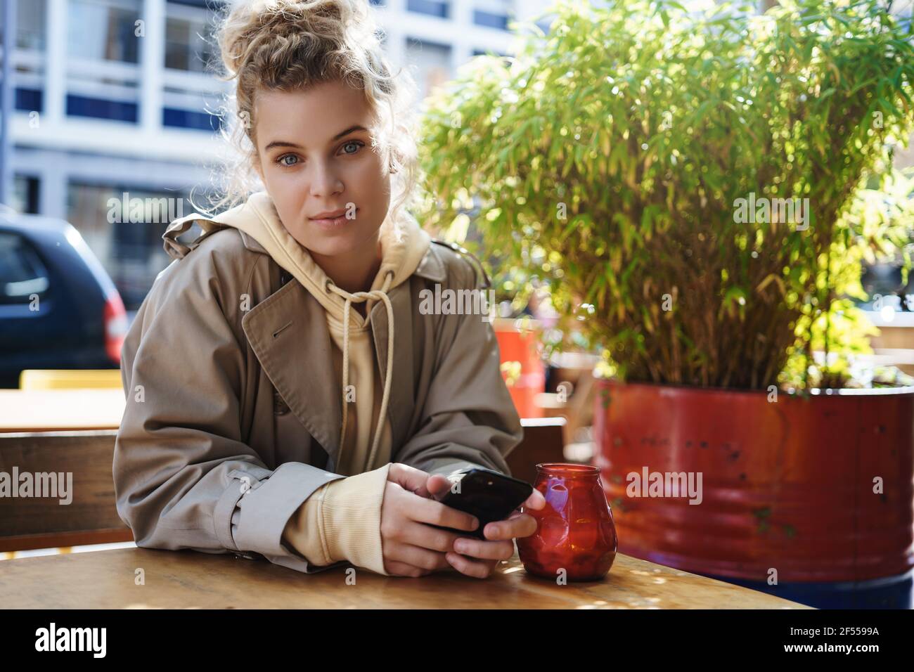 Young woman cafe client sitting outdoor and waiting for order, using ...