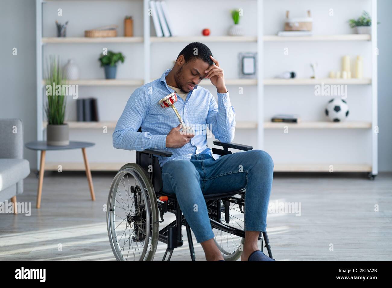 Portrait of sad black sportsman with trophy sitting in wheelchair ...