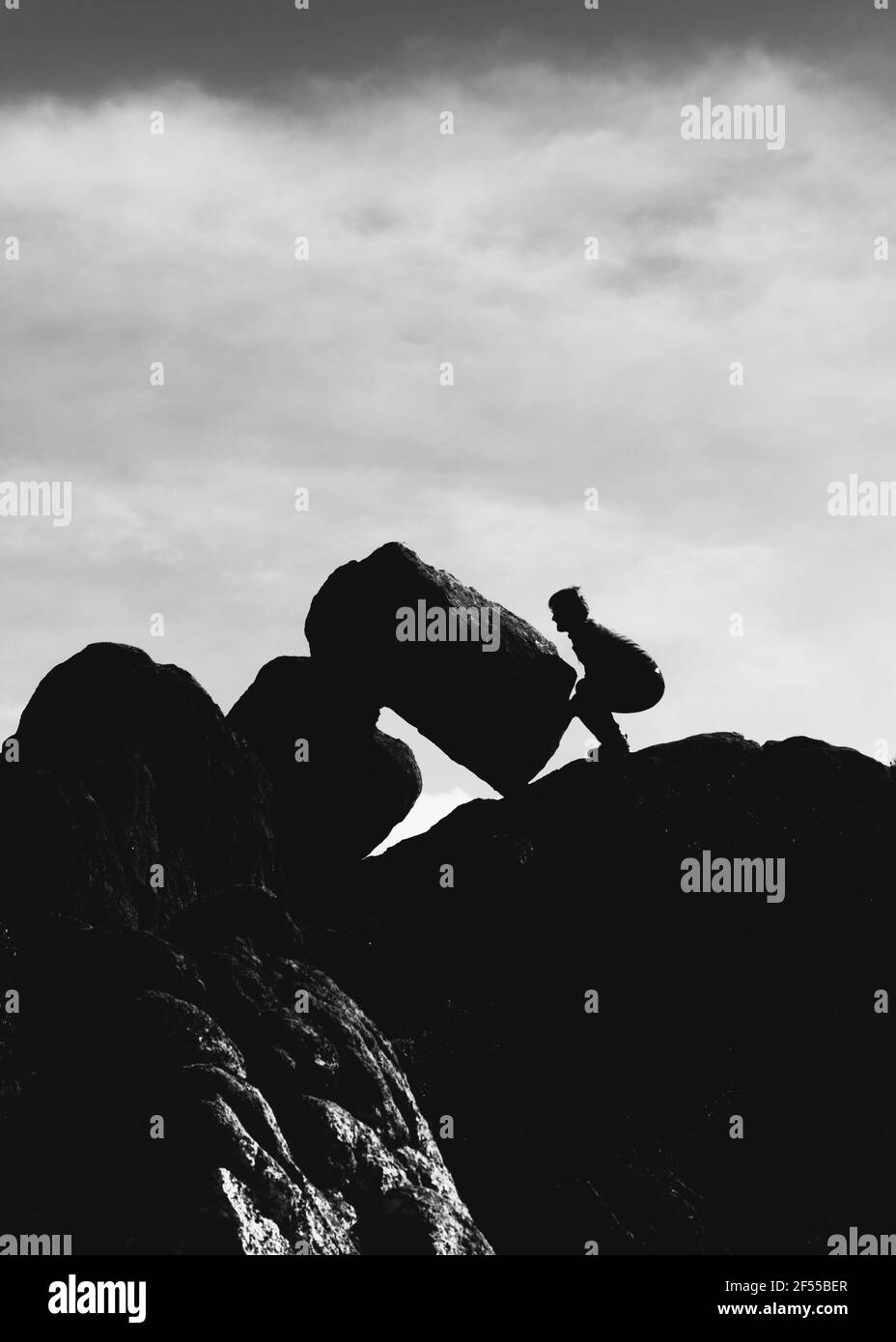 Silhouette man trying to lift a huge rock on top of a hill - goal or ...