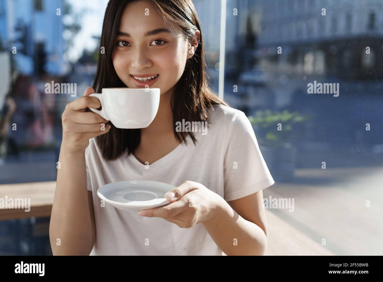 Woman in cafe drinking coffee near window on summer day. Girl sipping ...