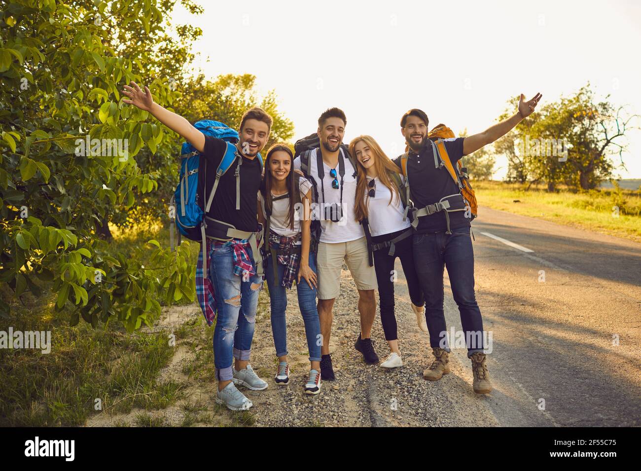 Group of young smiling tourists hikers standing on road together and ...