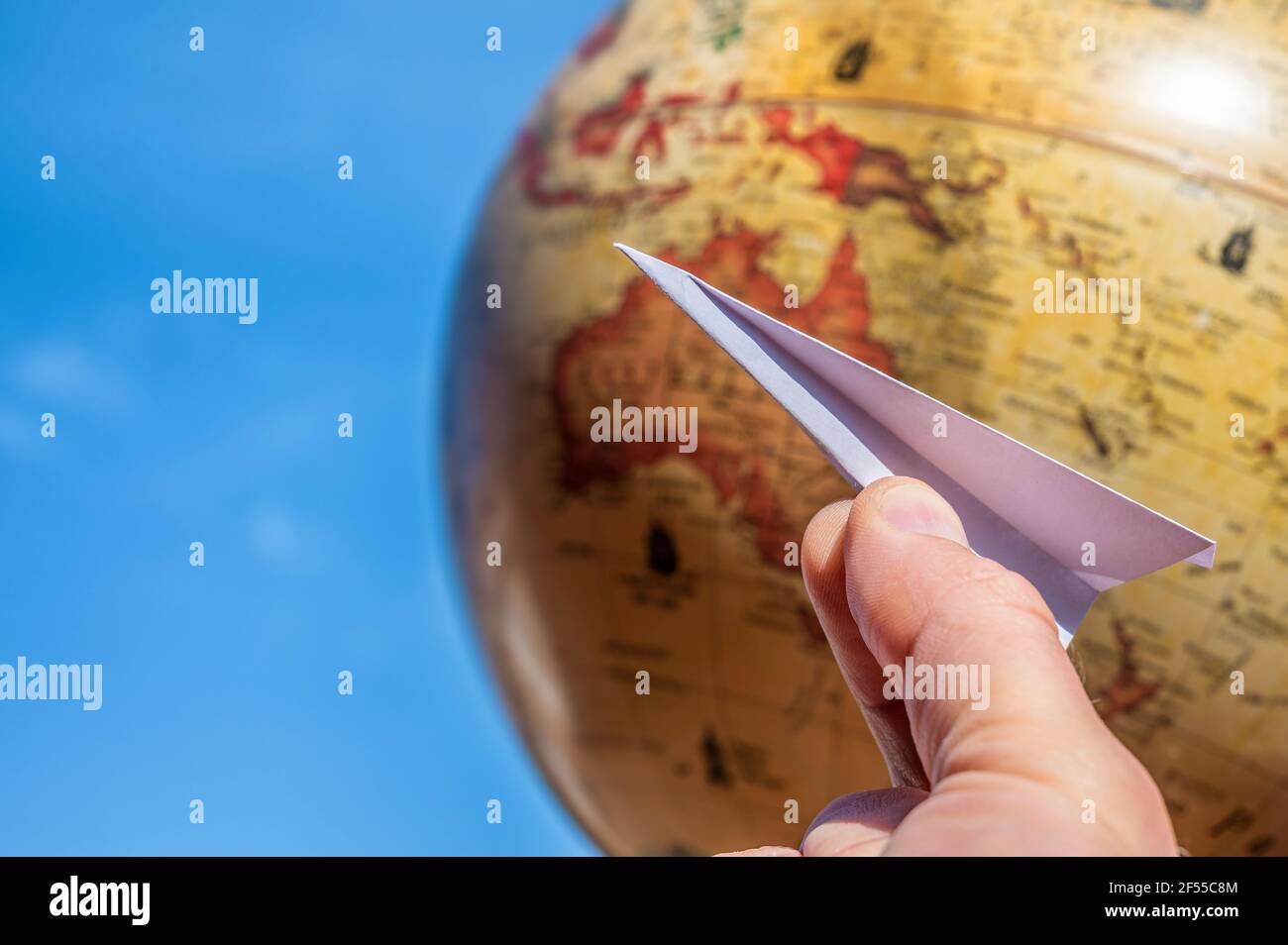 Paper airplane in front of a globe and blue sky symbolizing travel ...