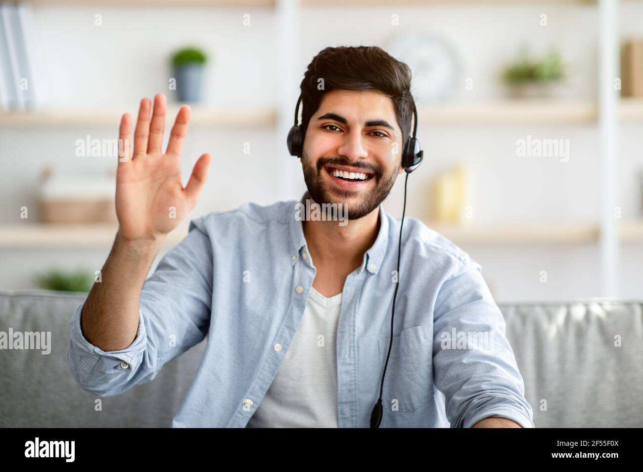 Greeting concept. Arab man wearing headset and waving hand to camera ...
