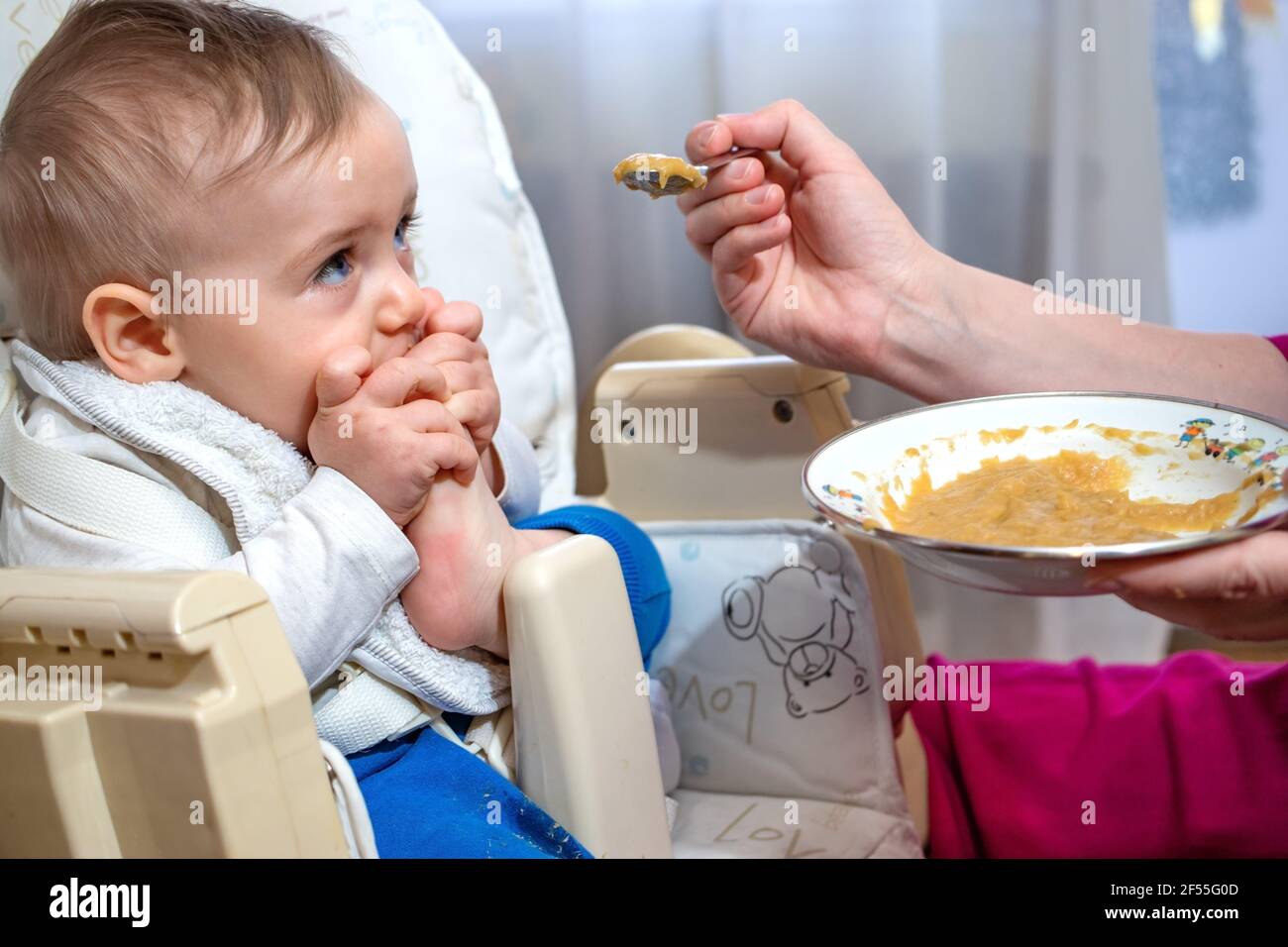 Baby boy sitting in a feeding chair, with his feet in the mouth instead ...