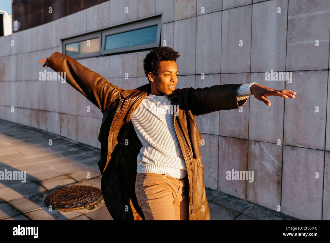 Smiling male dancer with arms outstretched dancing against building ...