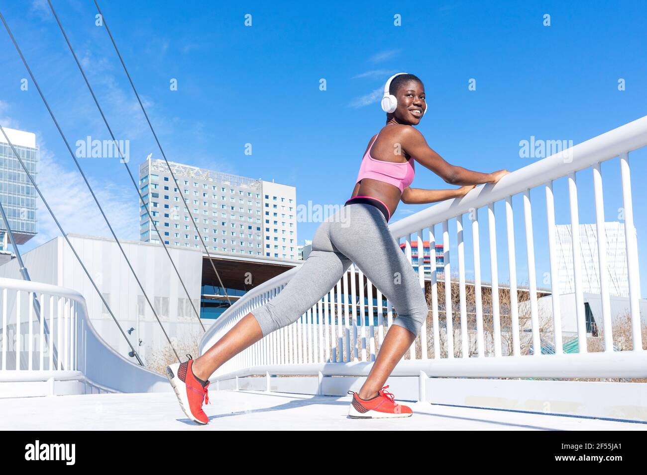 Smiling young woman listening music through headphones while stretching ...